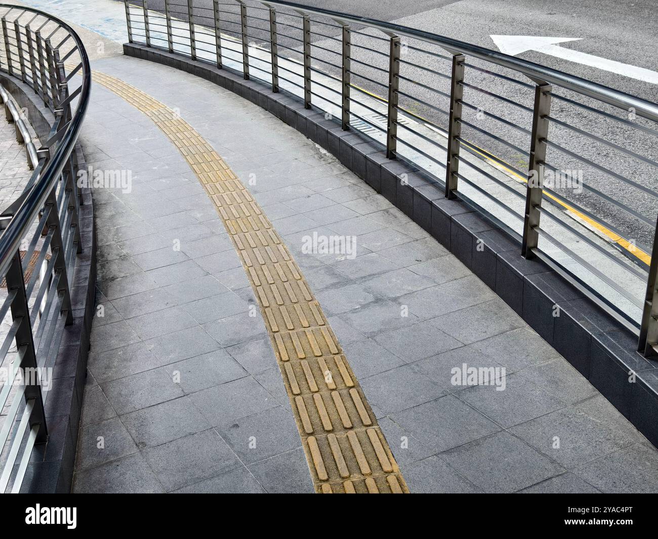 Curved path with guardrail and yellow line for blind people along the ...