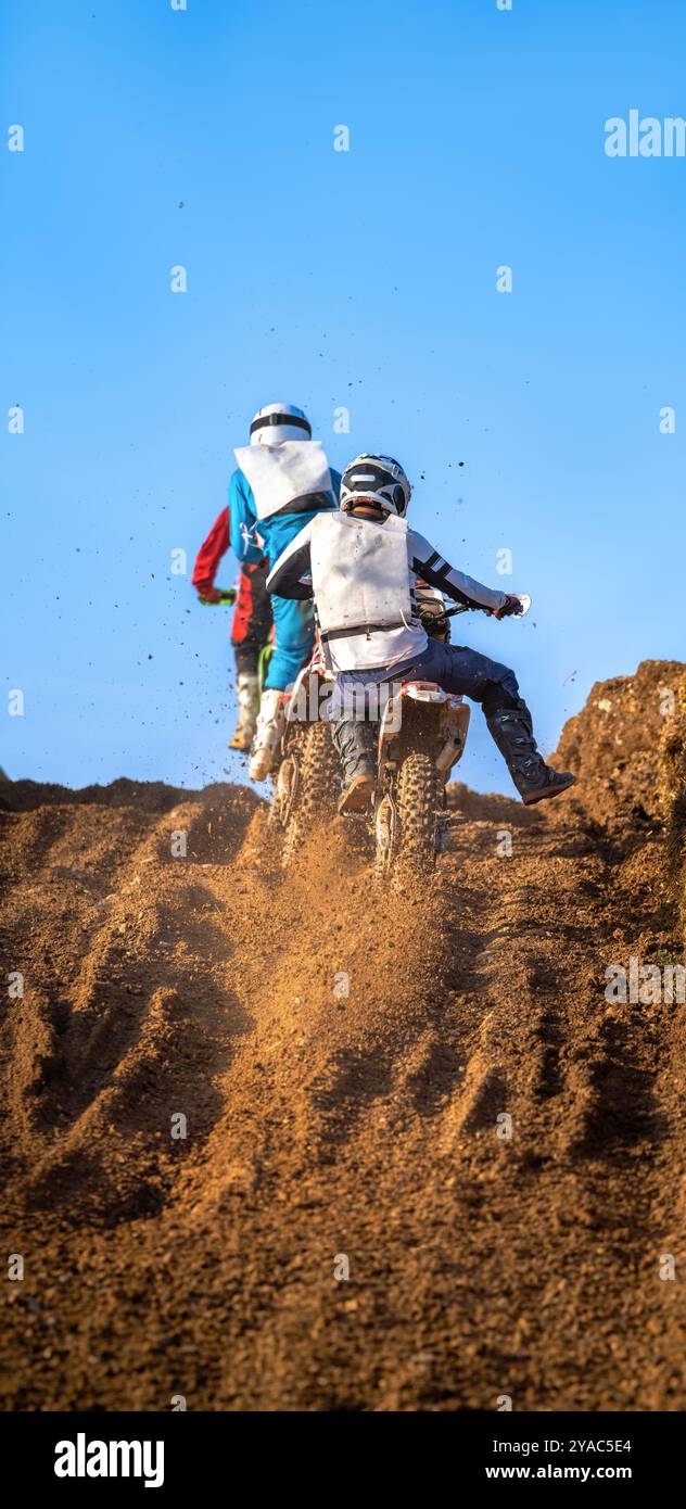 Motocross riders controlling their bikes as they climb a mud and gravel ...