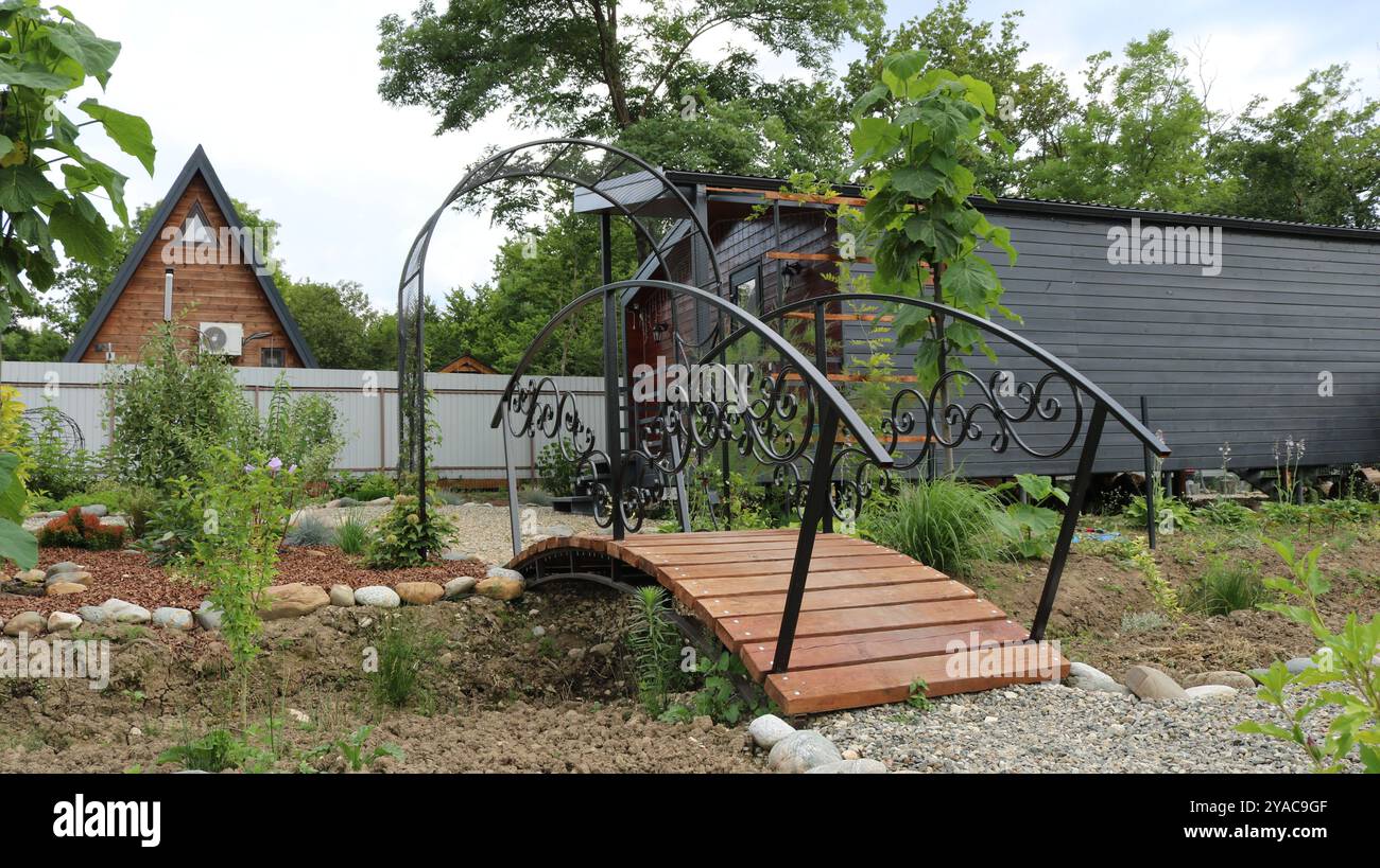 Arched small bridge of black metal and brown wood in a well-maintained ...
