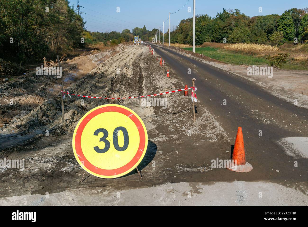 A road under construction with a large yellow circular speed limit sign ...