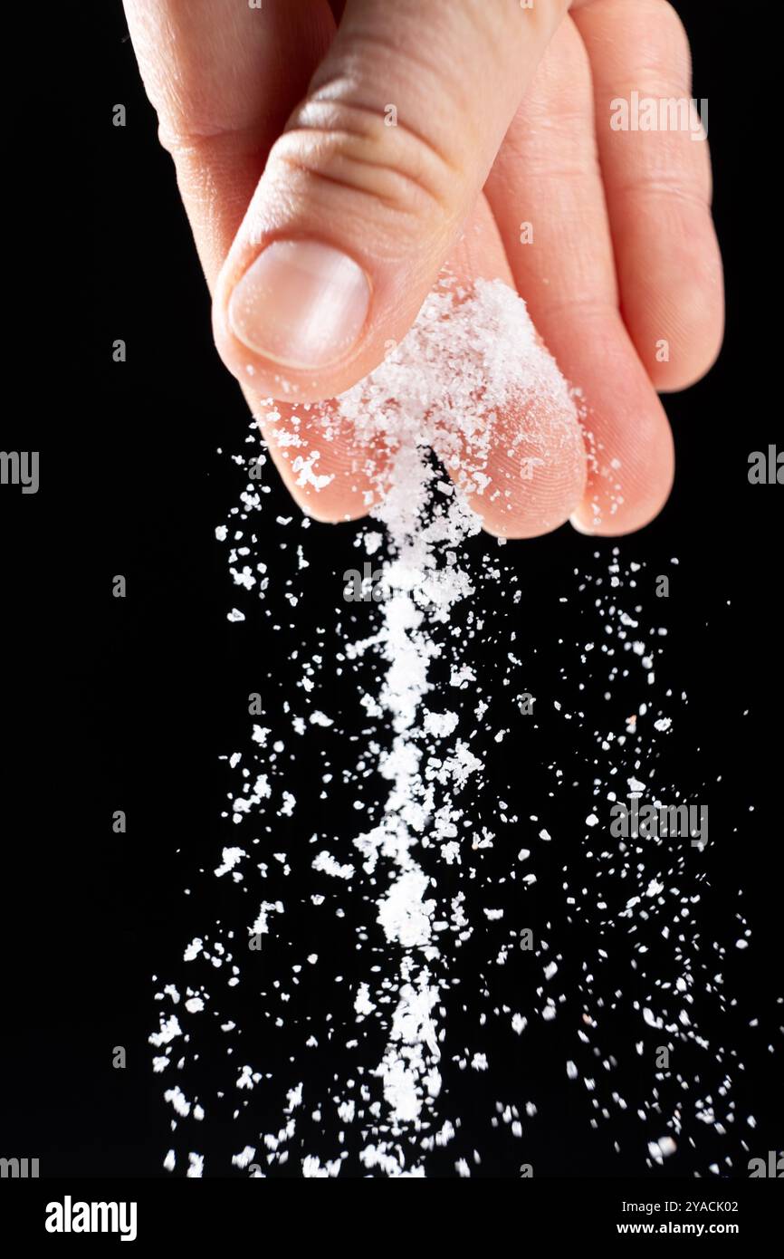 Hand pouring white stone salt finely ground, black background Stock ...