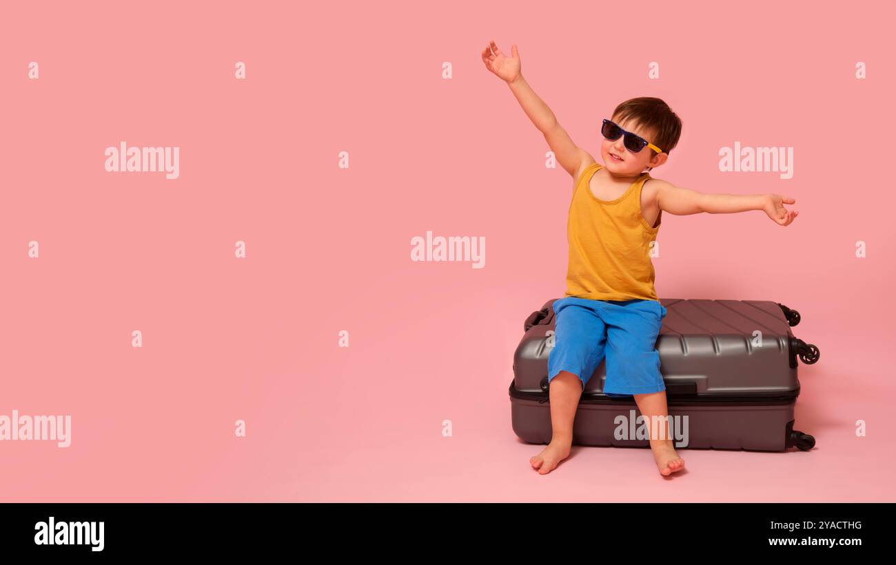 Happy child is seated on a pink suitcase, prepared for a long journey ...