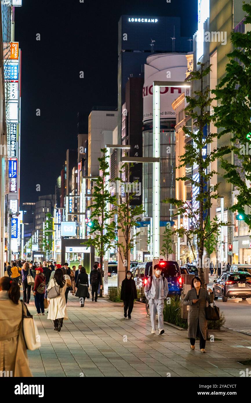 People walking along the brightly lit Ginza shopping street at night ...