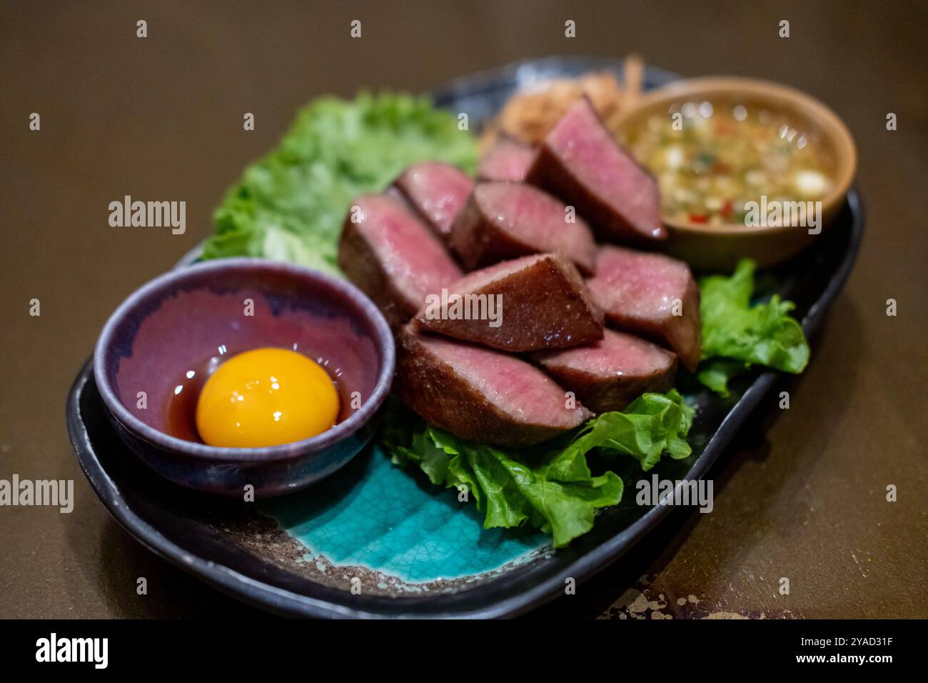 Grilled beef tongue served on plate with pickled egg yolk and sauce ...