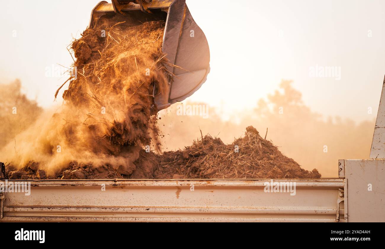 Backhoe loading soil into heavy duty dump truck at construction site ...
