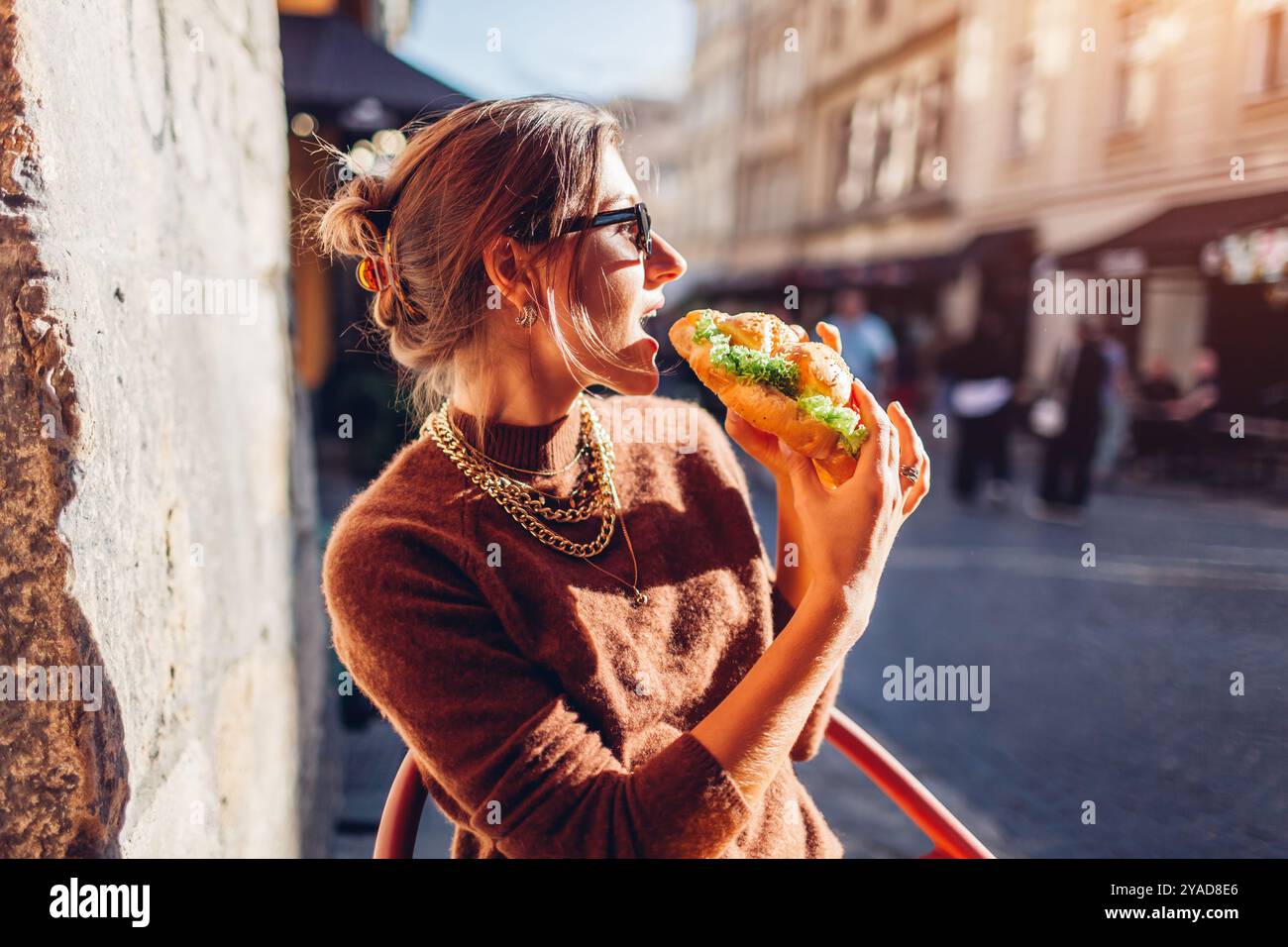 Young woman having fresh croissant in outdoor cafe at sunset. Customer ...