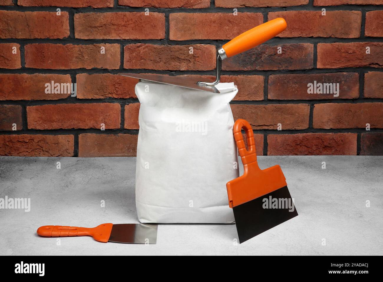 Bag of cement and trowels on light textured table against red brick ...