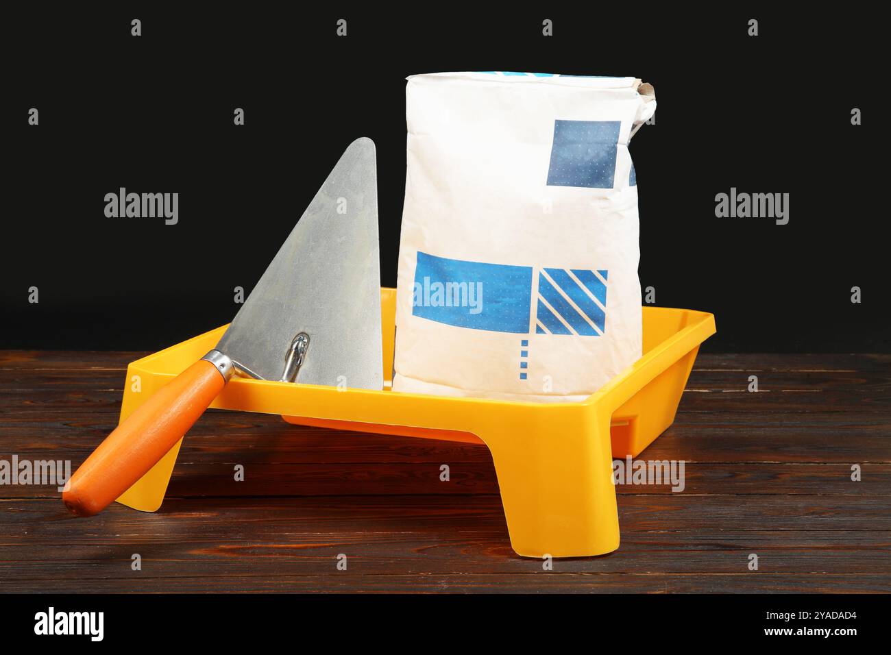 Bag of cement powder, tray and putty knife on wooden table. Building ...