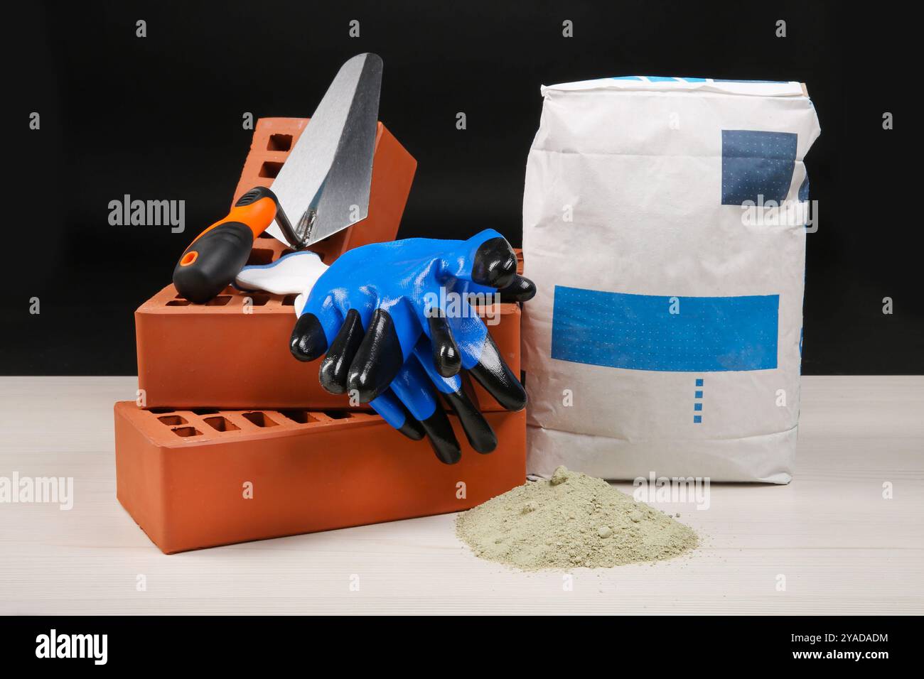 Red bricks, cement powder, putty knife and gloves on light wooden table ...