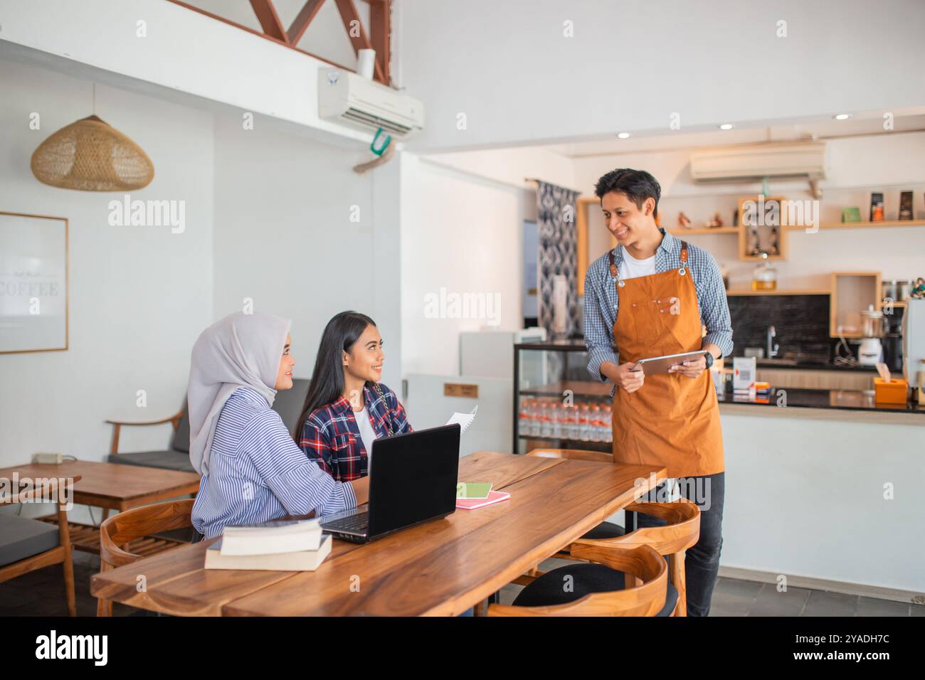 two Indonesian women use laptop and order drinks from male waiter Stock ...