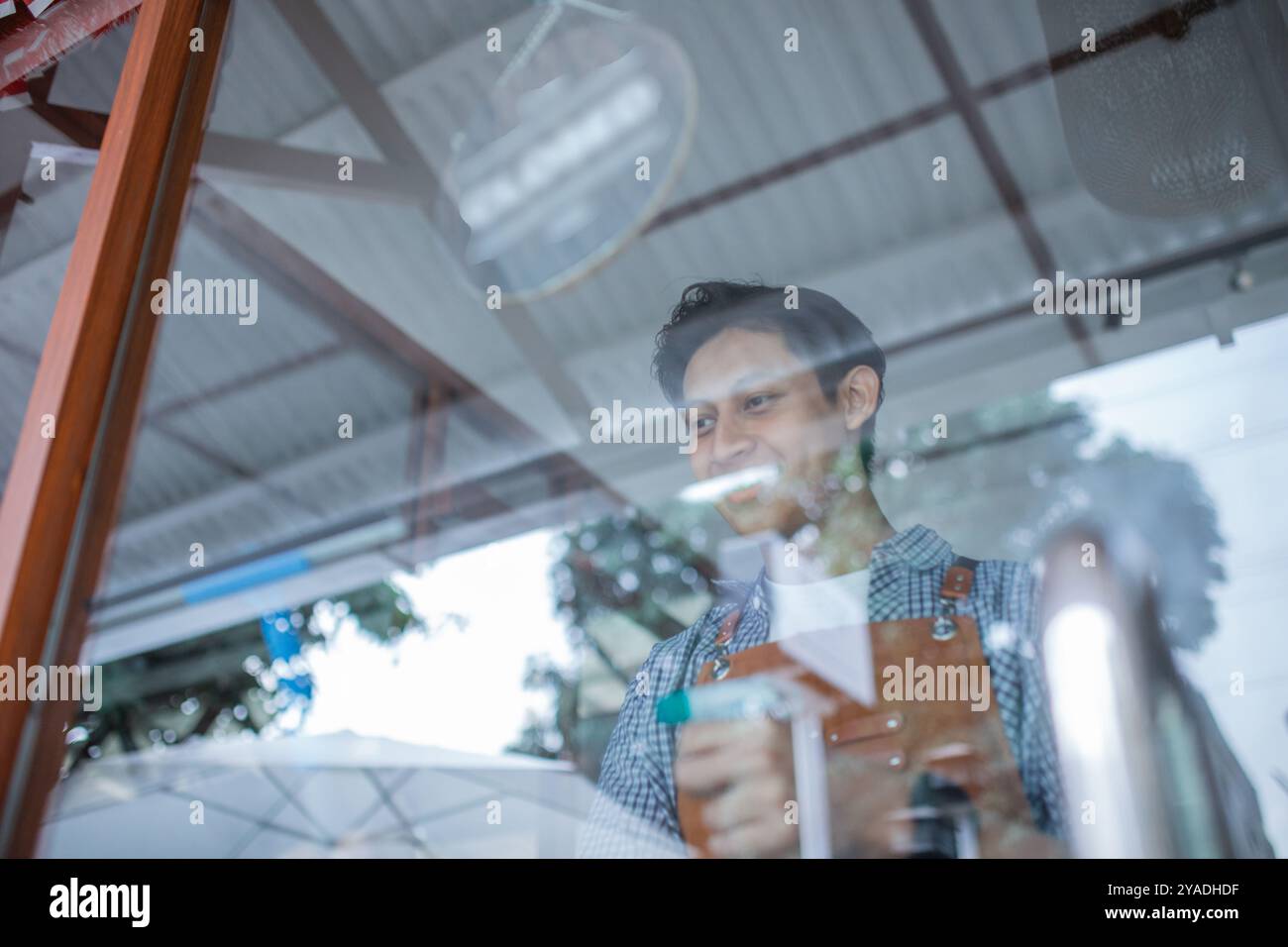 male waiter wearing apron cleaning glass window with wiper and spray ...