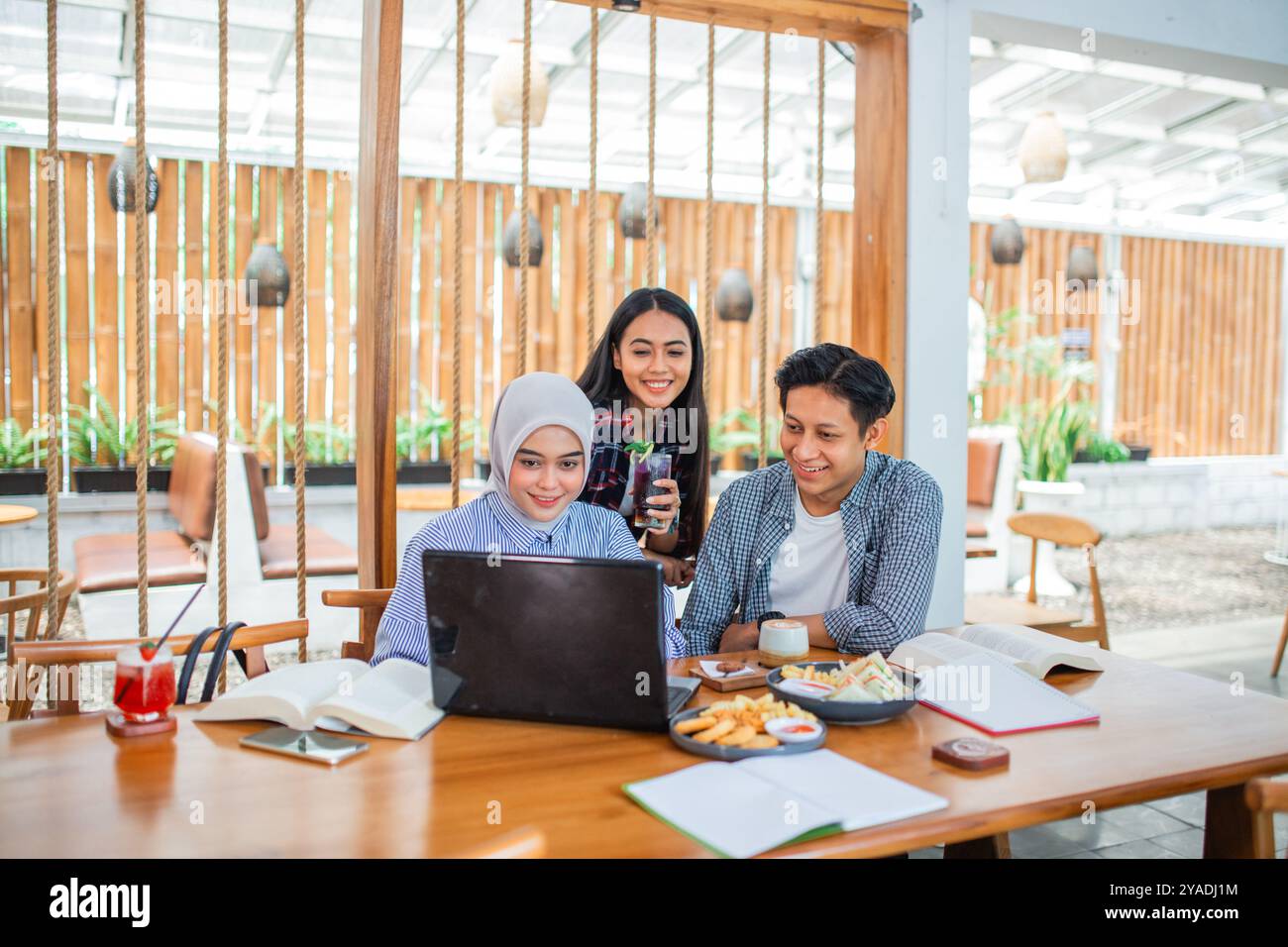 three university students use and look at a laptop together Stock Photo ...