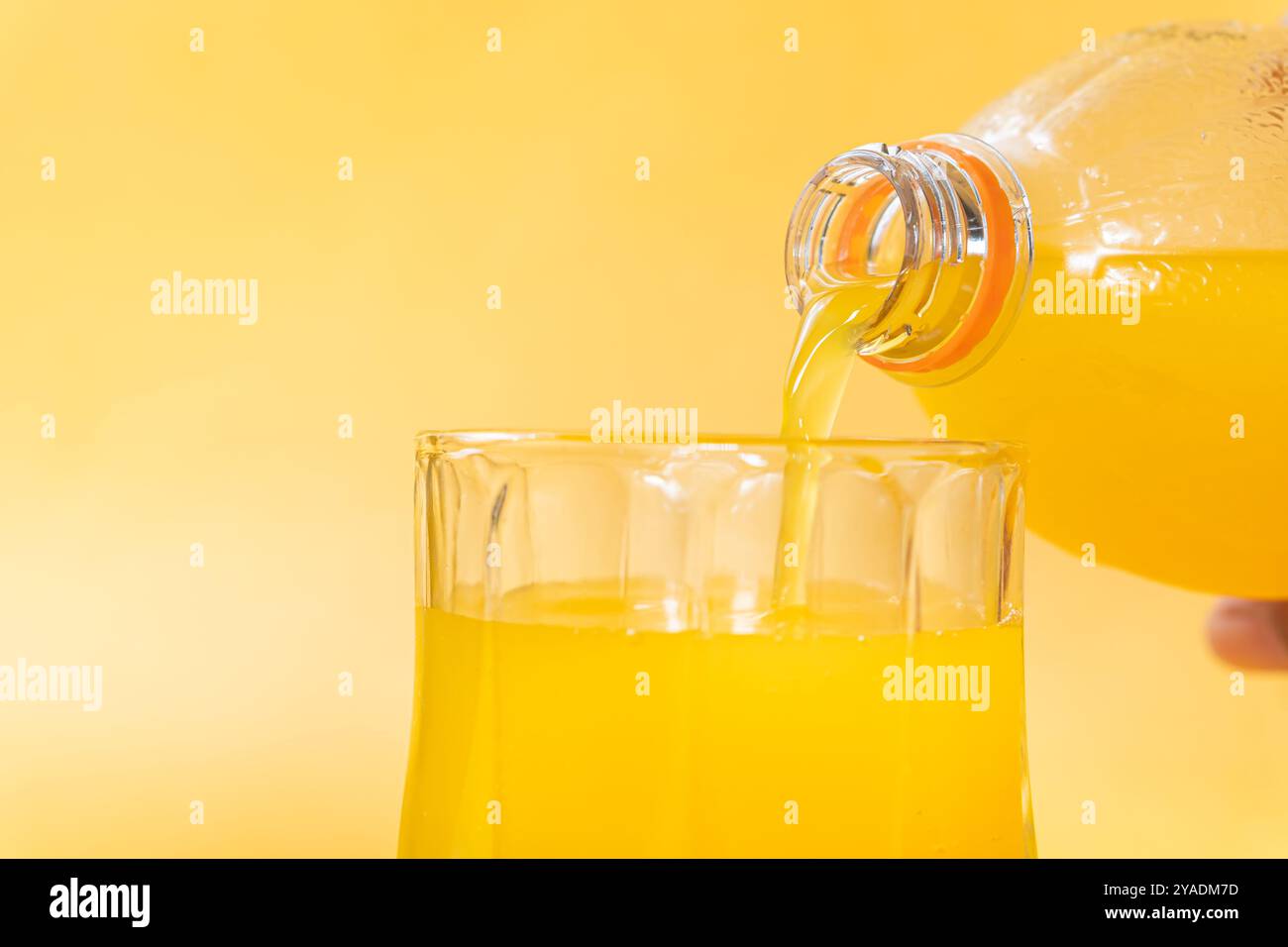 A close-up of a bottle pouring orange juice into a clear glass. The ...