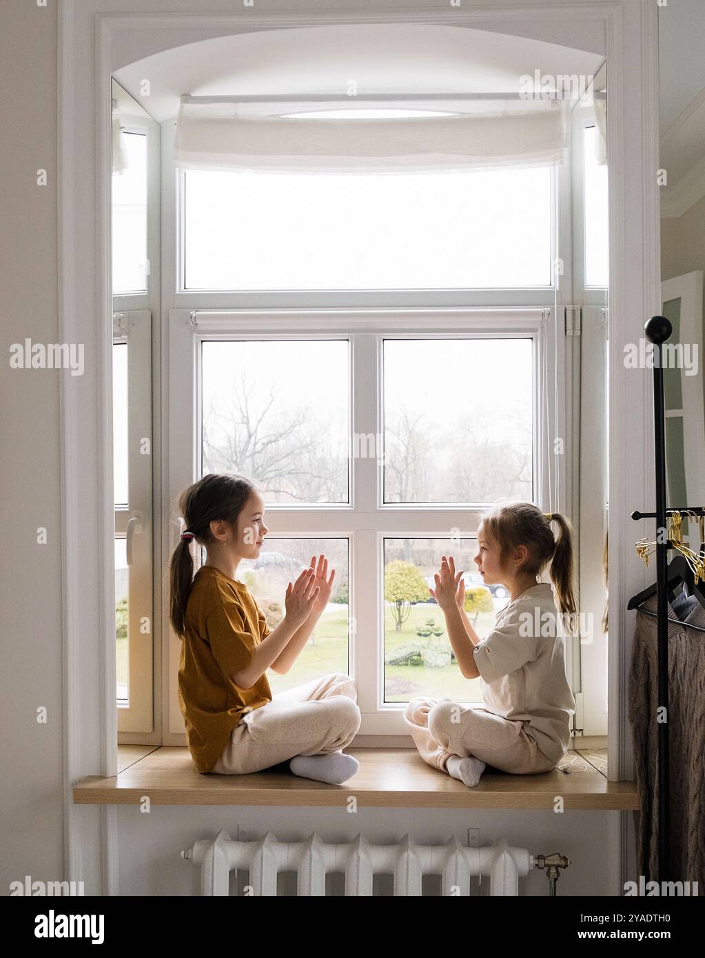 wo young girls sit on a windowsill, engaged in a playful game of ...