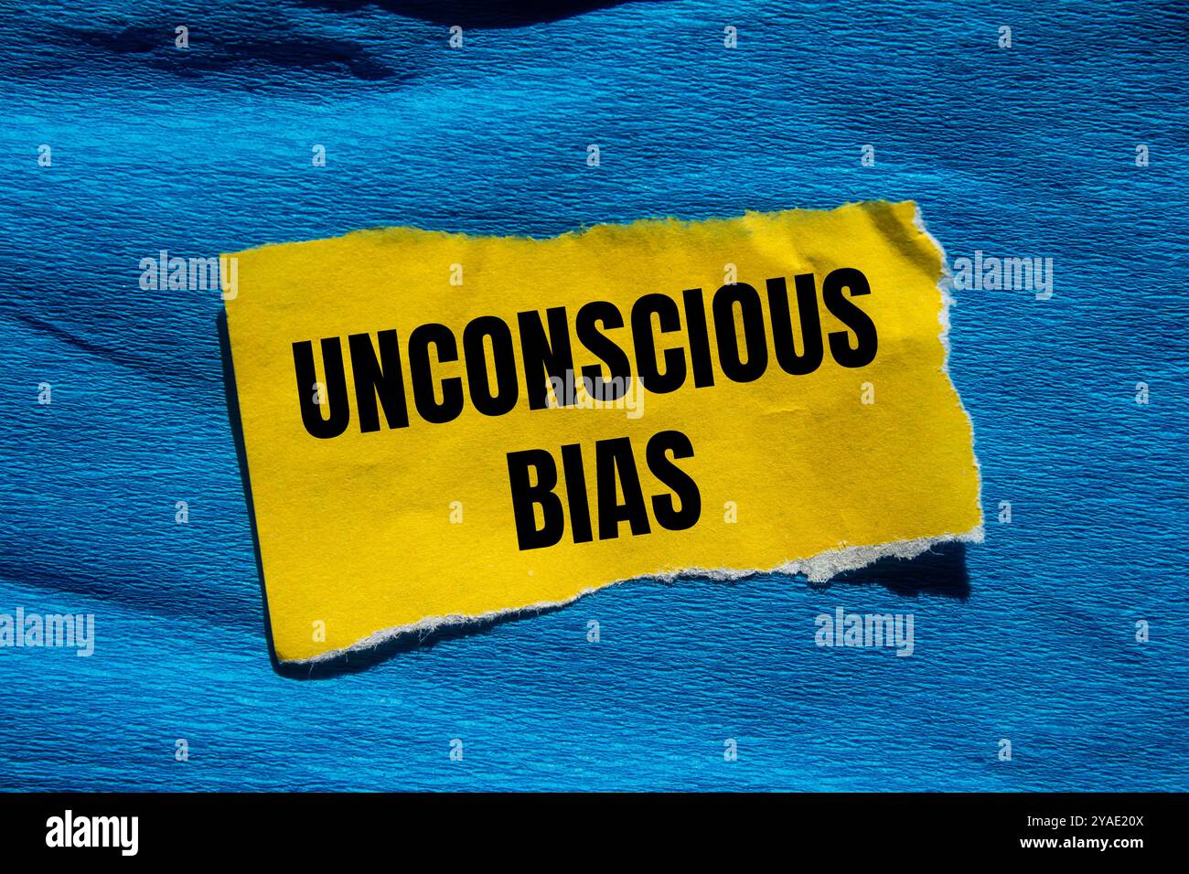 Unconscious bias message written on ripped torn yellow paper piece with blue background ...
