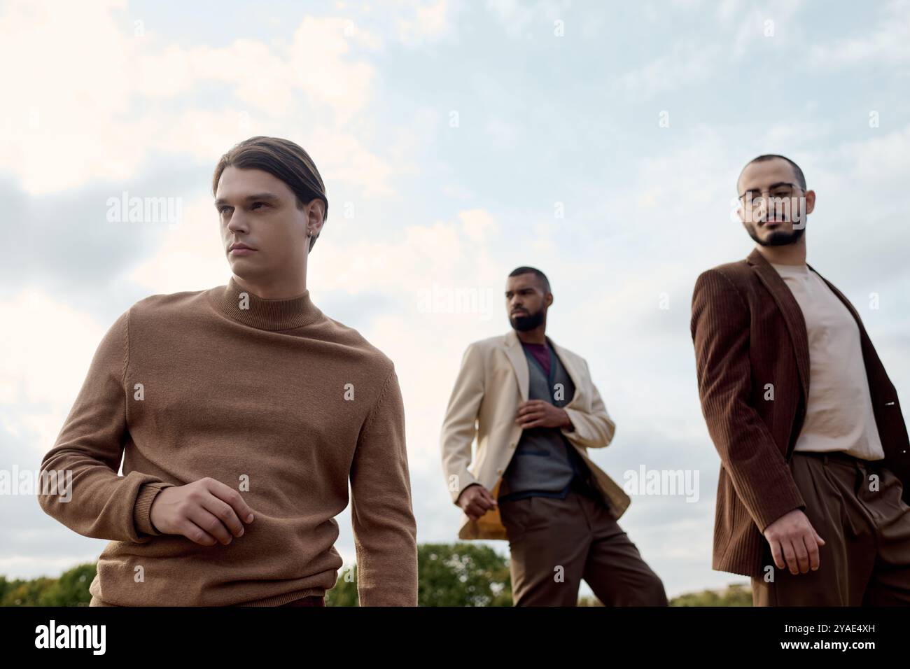 Three stylish men confidently pose in a scenic autumn field, embodying ...