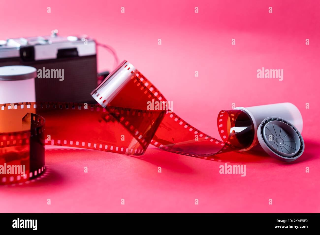 A vintage camera with rolls of red film on a bright pink background ...