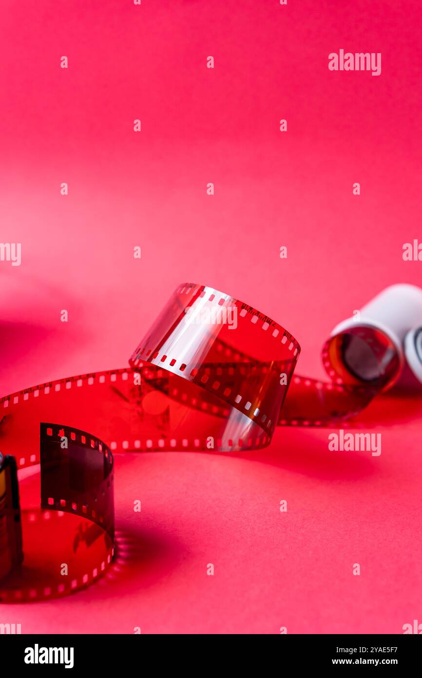 A close-up of a red film strip coiled on a vibrant pink background. The ...