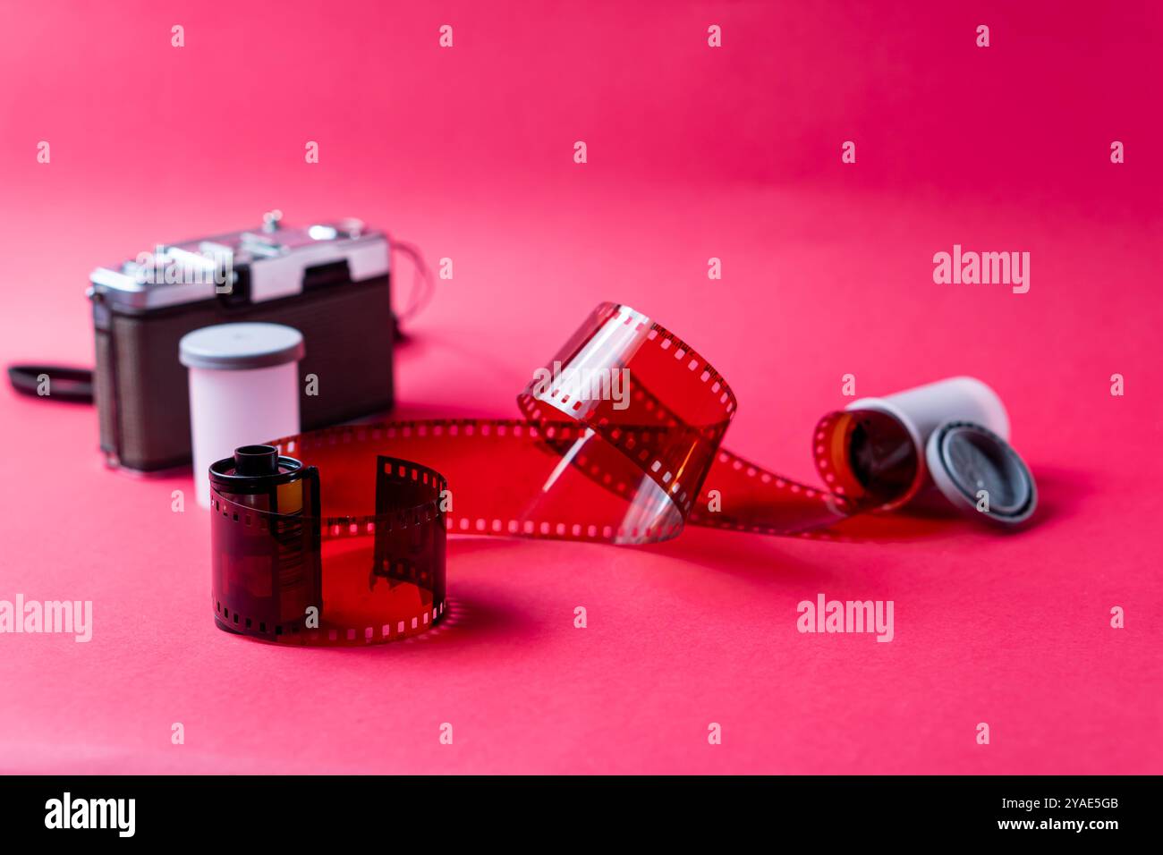 A vintage camera with rolls of red film on a bright pink background ...