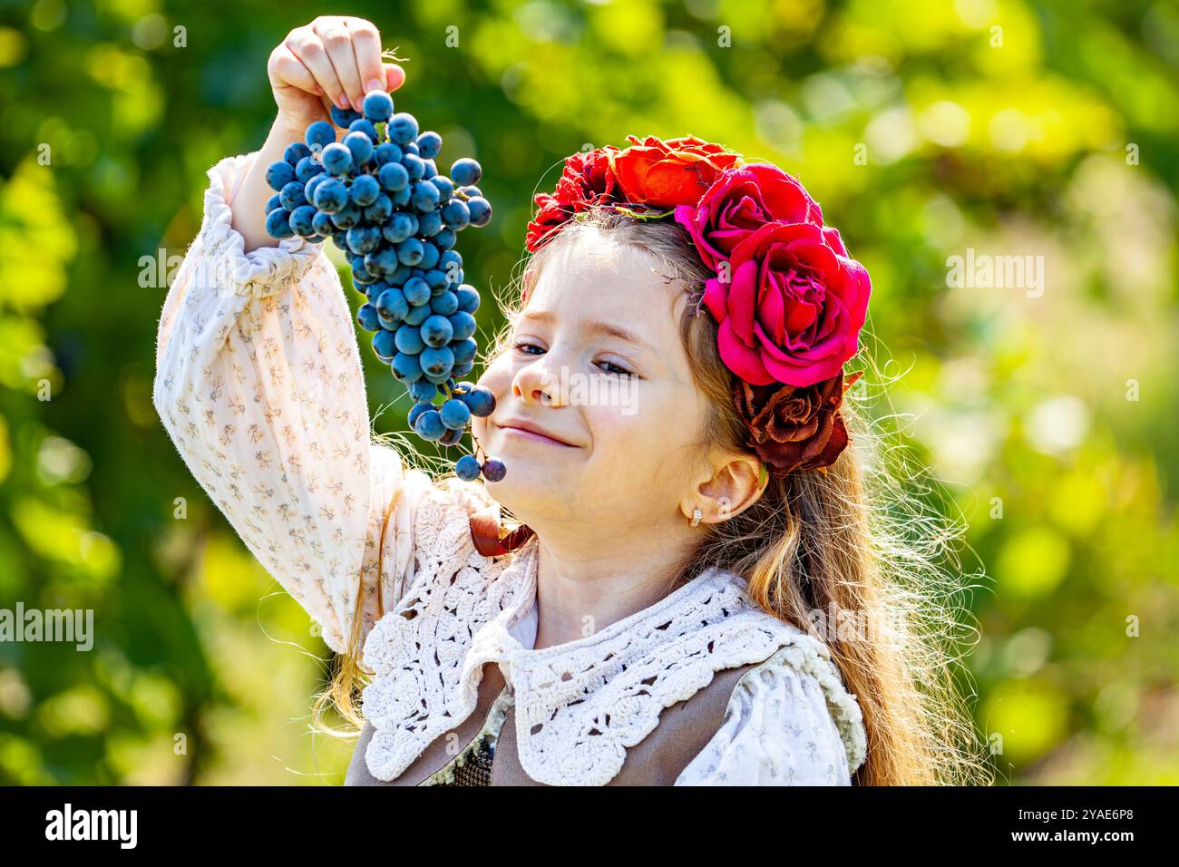 Smiling kid girl 4-5 year old eating fresh grapes outdoors. Looking at ...