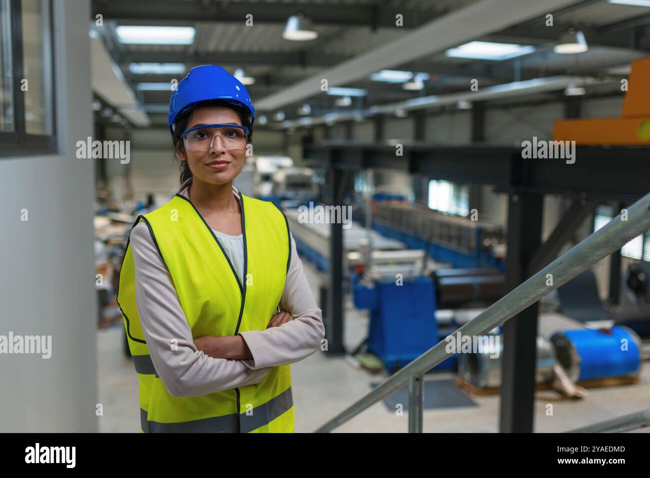 Female industrial plant employee with a blue helmet and yellow vest in ...