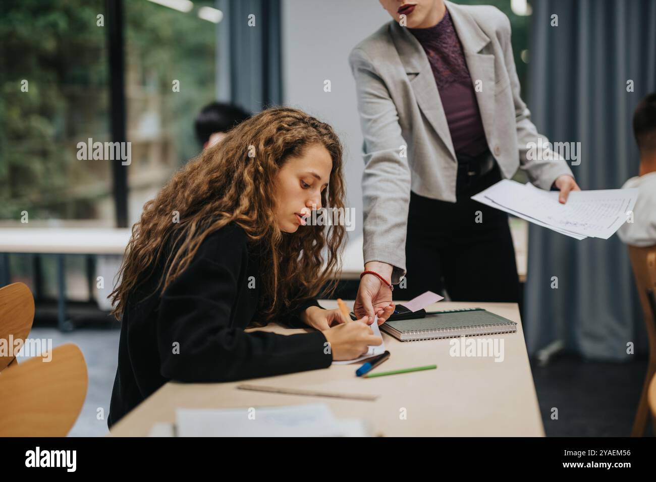 Focused student writing notes in classroom with teacher guidance Stock ...