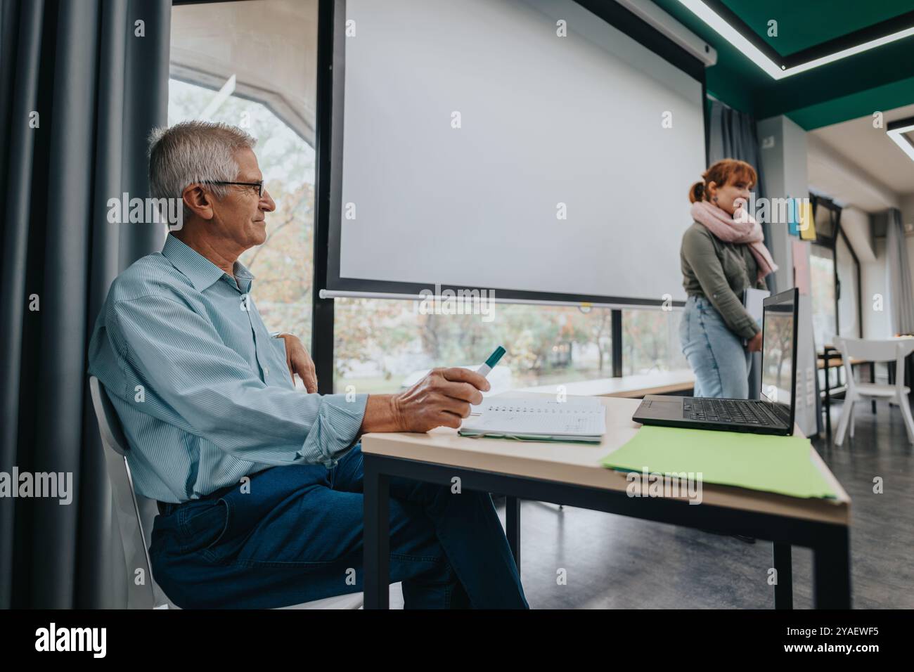Elderly professor engaging with students in a modern classroom setting ...