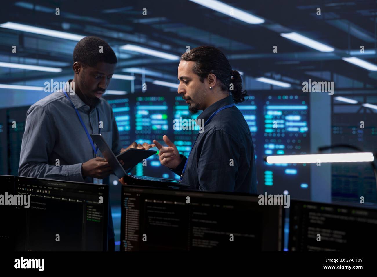 Engineers in data center using tablet and laptop to check for server performance issues arising ...