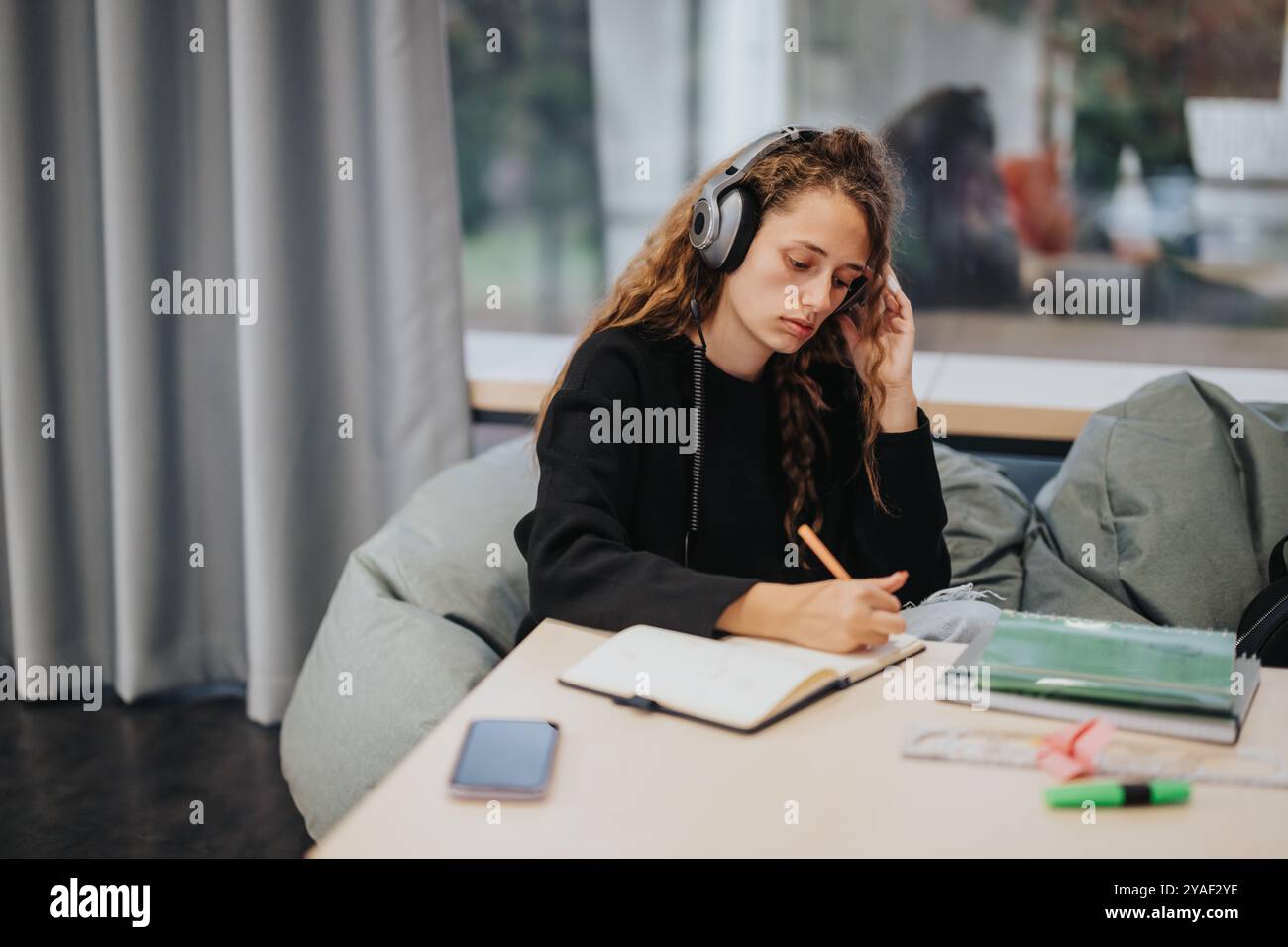 Focused high school student studying with headphones in library Stock ...
