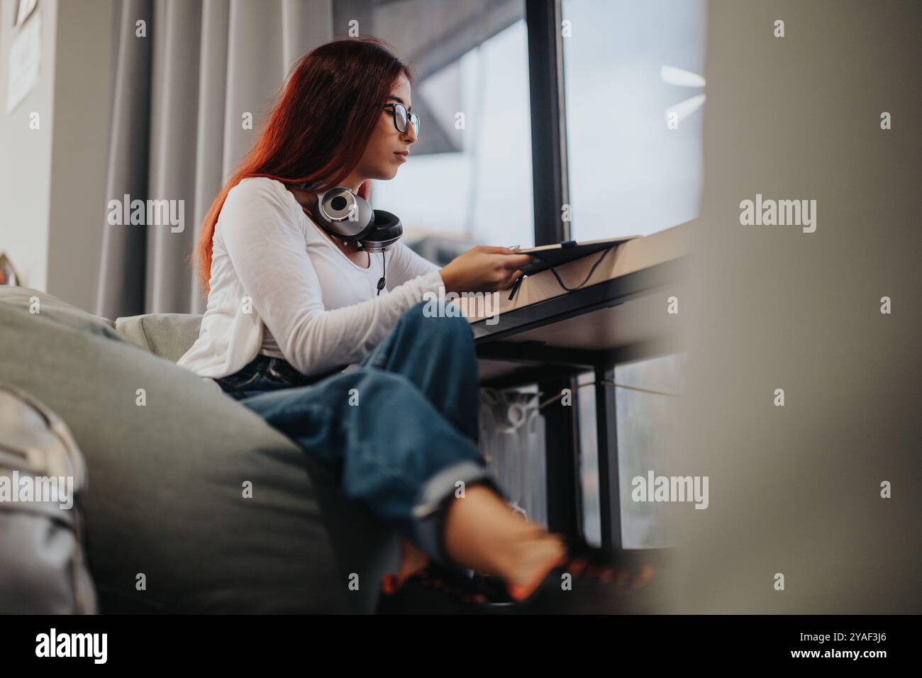 High school student studying by window with tablet and headphones Stock ...