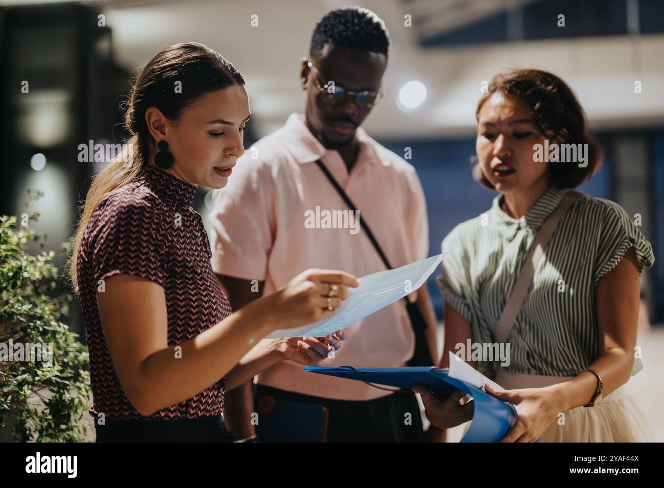 Three young professionals reviewing documents outdoors at night ...