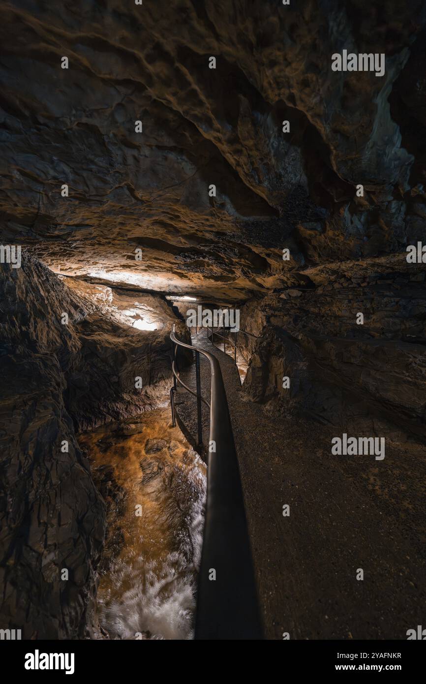 Narrow path in an illuminated cave with flowing water, gloomy adventure ...