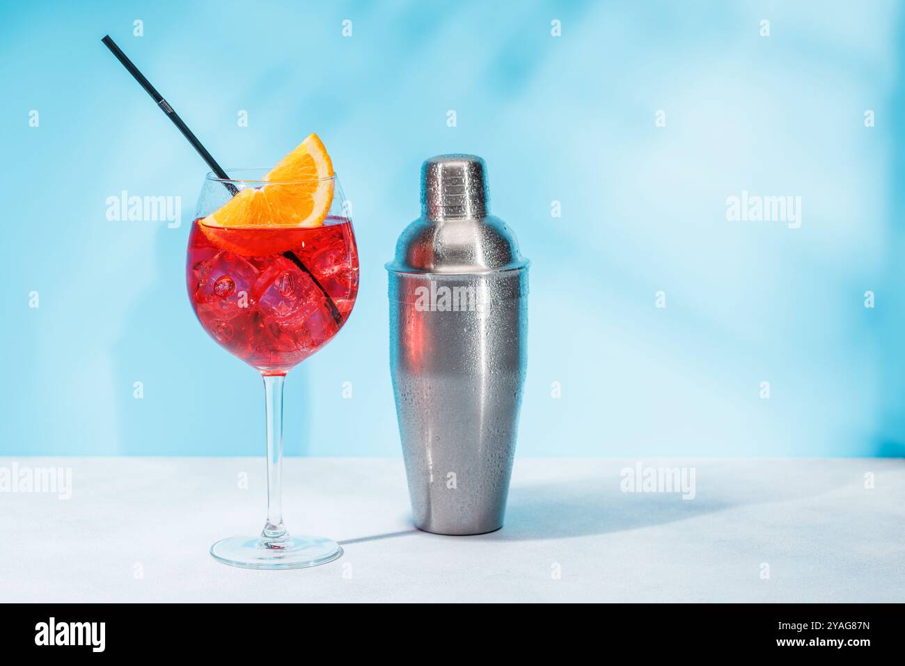 A cocktail and cocktail shaker arranged on a table against a light blue ...