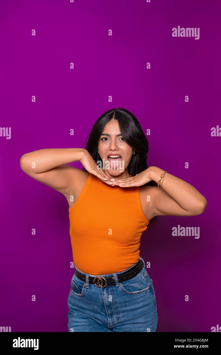 Cheerful woman in orange top and jeans, playfully sticking out tongue ...