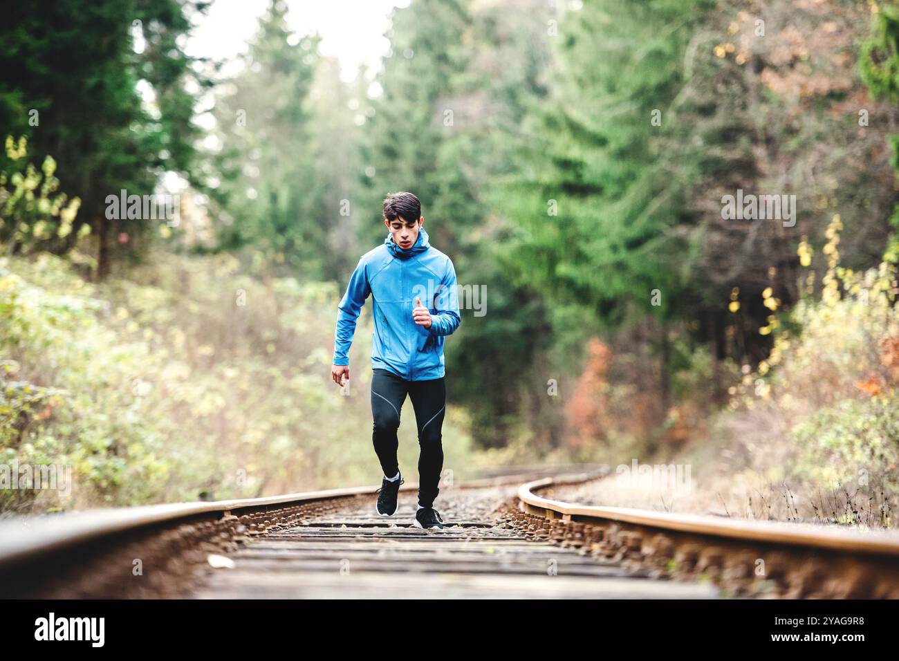 Sporty man running on old unused rails in the middle of nature. Morning ...