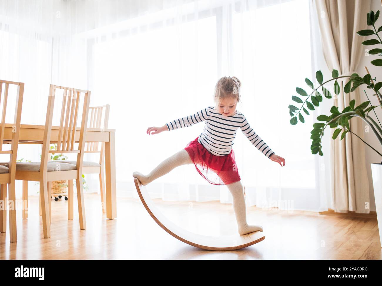 Little girl balancing on wooden wobble board. Girl is playing on wooden ...
