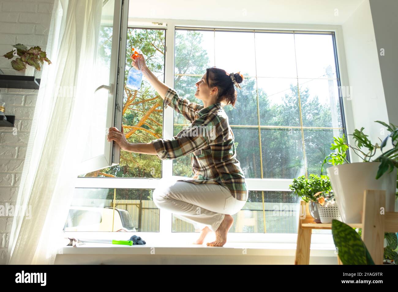 Woman manually washes the window of the house with a rag with spray ...
