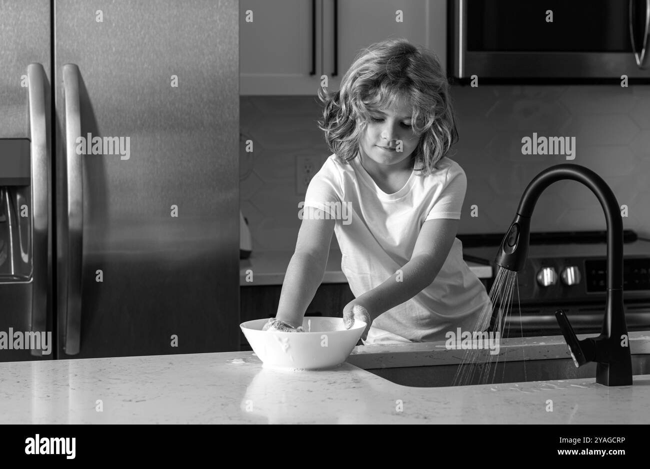 Kid boy washing dishes in the kitchen interior. Child helping his ...