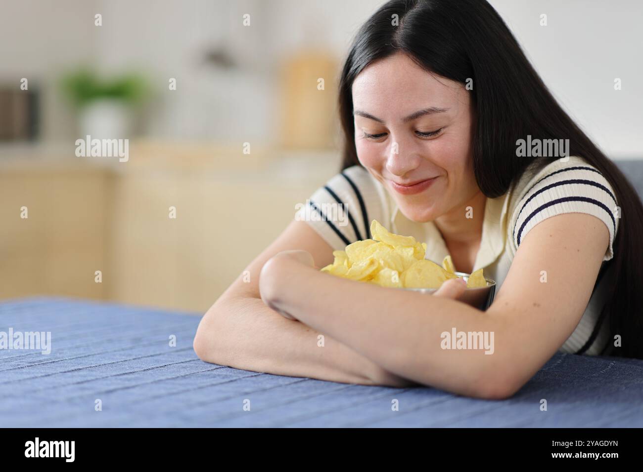 Gluttonous asian woman ready to eat potato chips in the kitchen at home ...