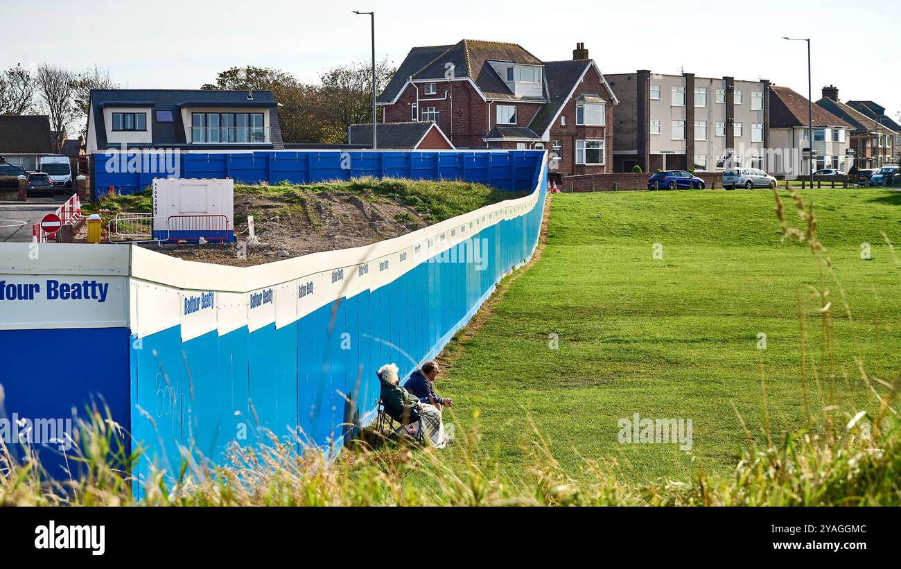 Couple sat in folding chairs up against construction site compound with ...
