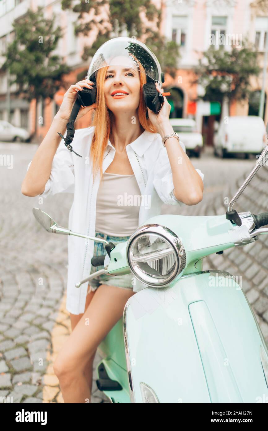 Young woman putting on helmet for moped ride Stock Photo - Alamy