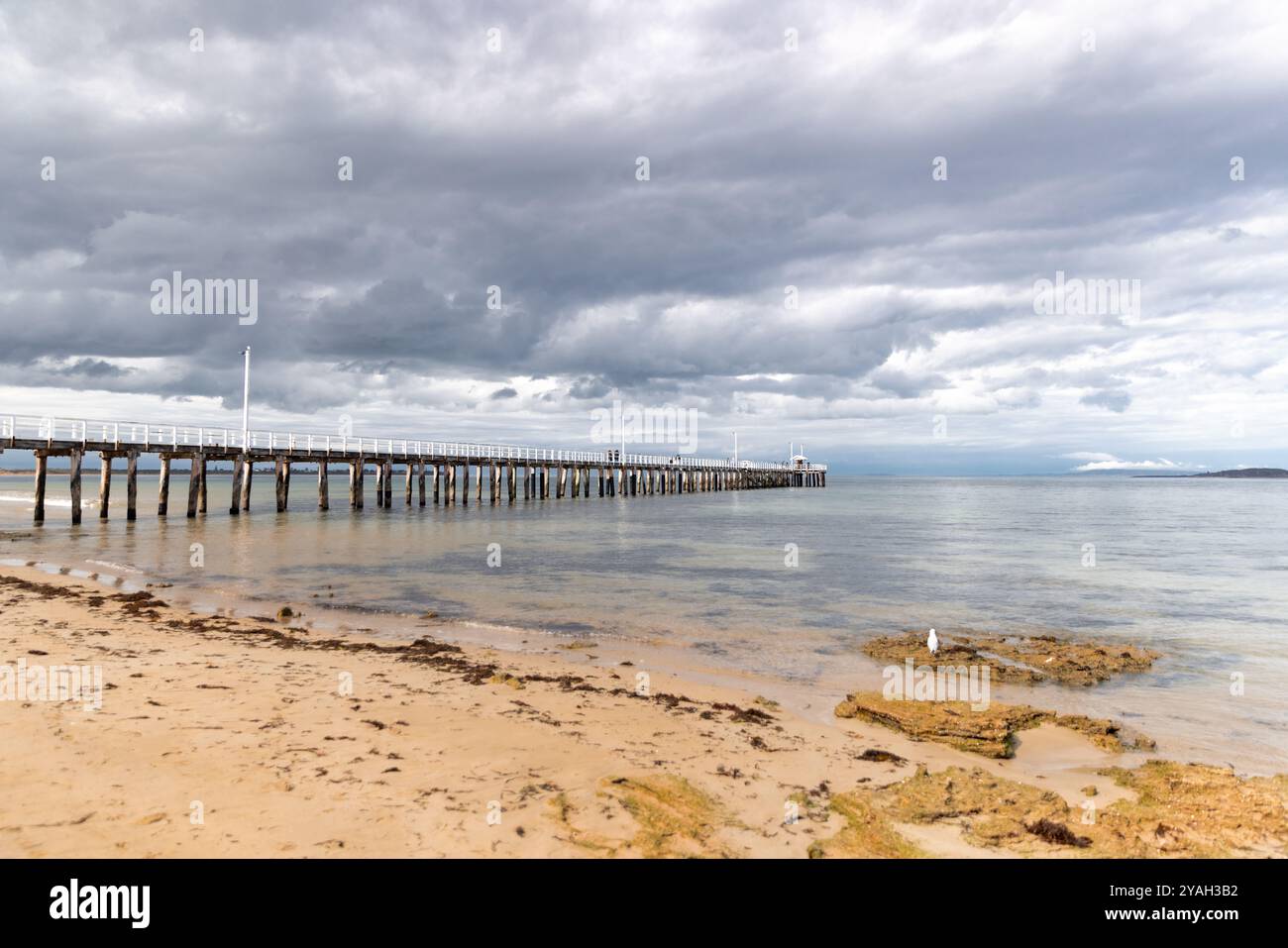 Point Lonsdale Pier stretching out into calm ocean under a cloudy sky ...