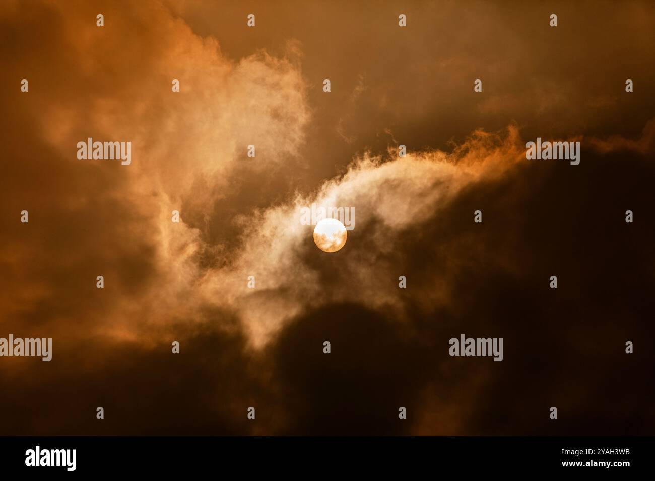 The sun burns a bright round circle through smokey clouds Stock Photo ...