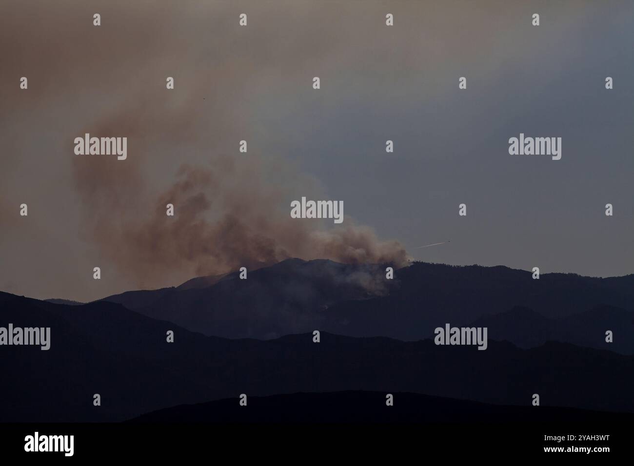 Smoke rising from mountainous wildfire distant plane trailing away ...