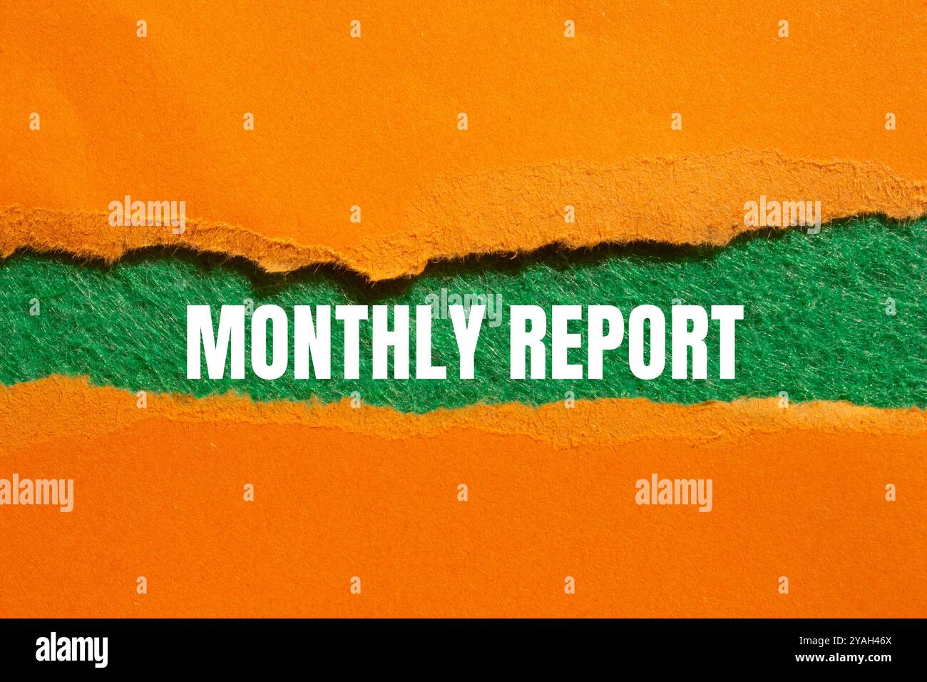 Monthly report message written on ripped torn orange paper with green background. Conceptual ...