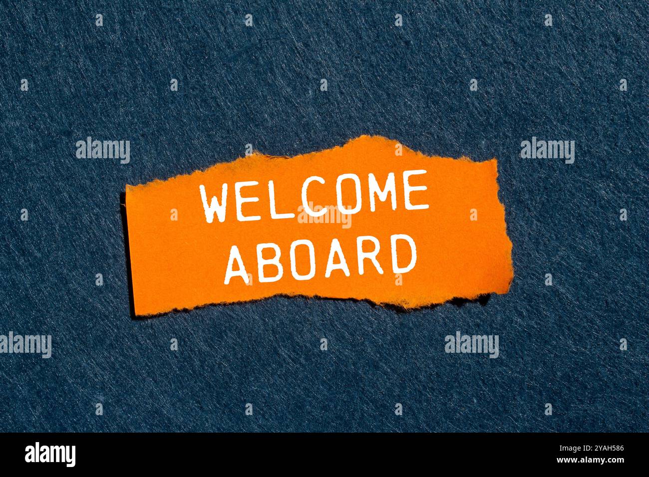 Welcome aboard message written on ripped torn orange paper piece with gray felt background ...