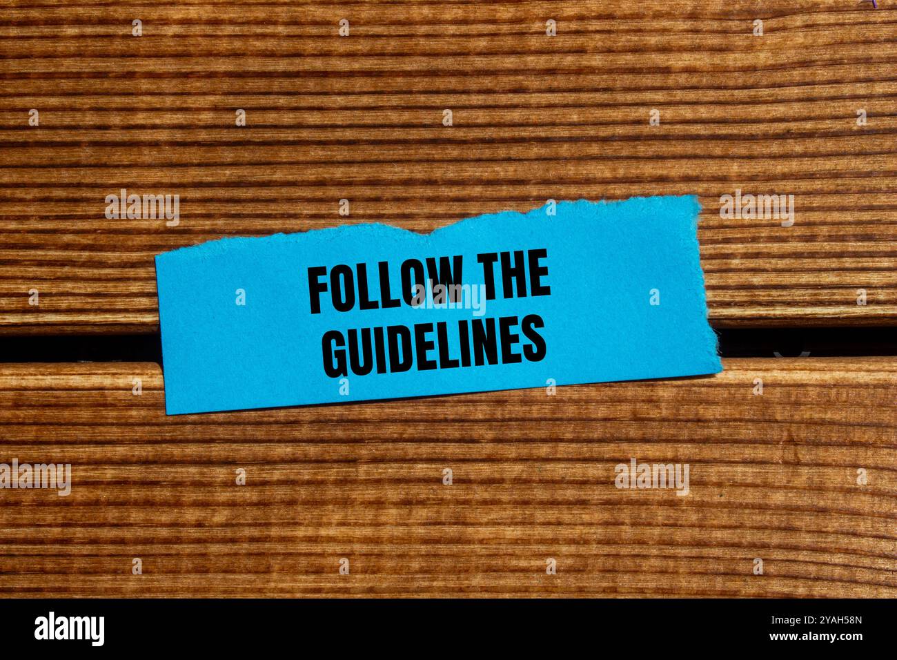 Follow the guidelines message written on ripped torn blue paper piece with wooden background ...