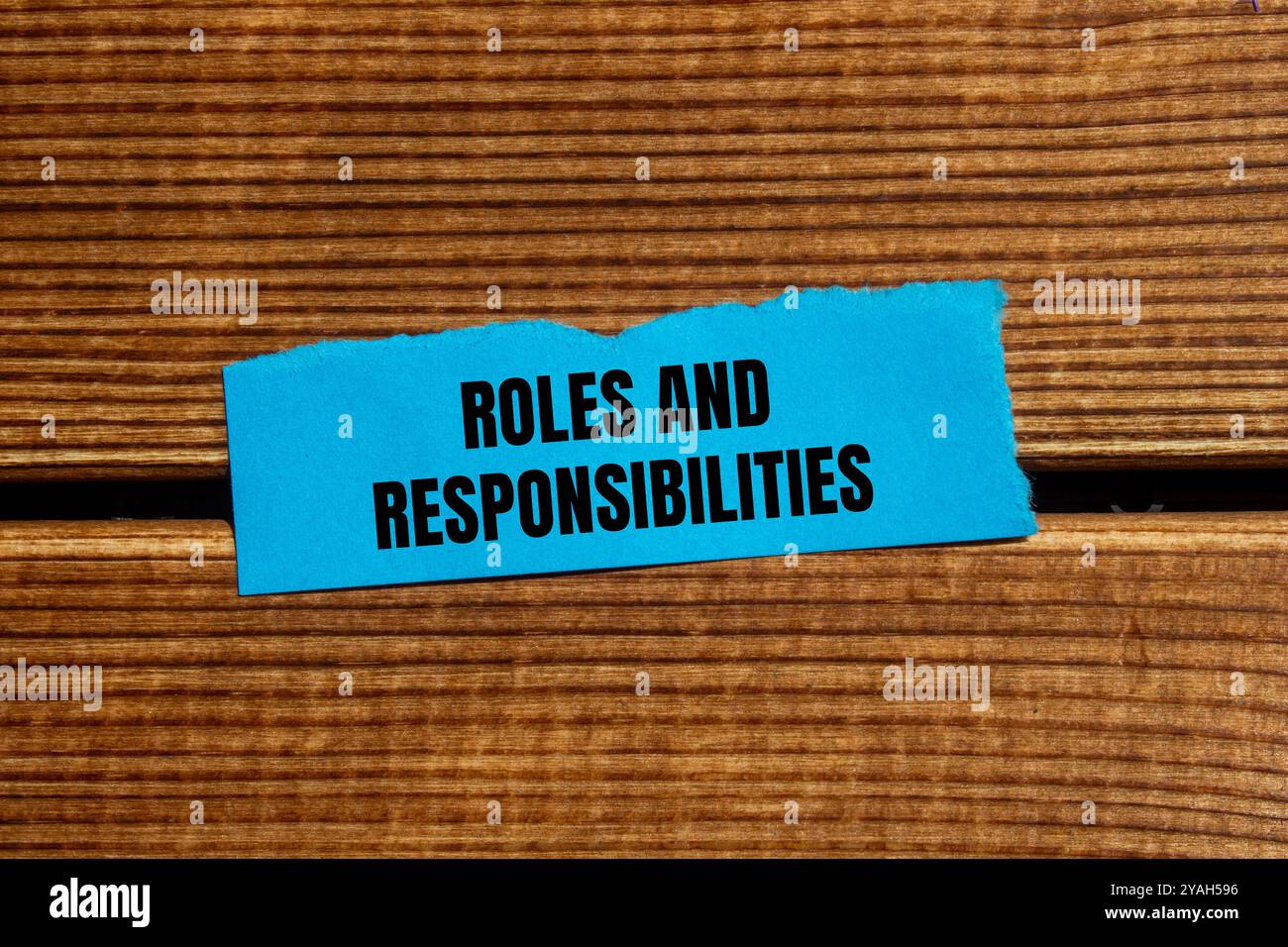 Roles and responsibilities message written on ripped torn blue paper piece with wooden ...