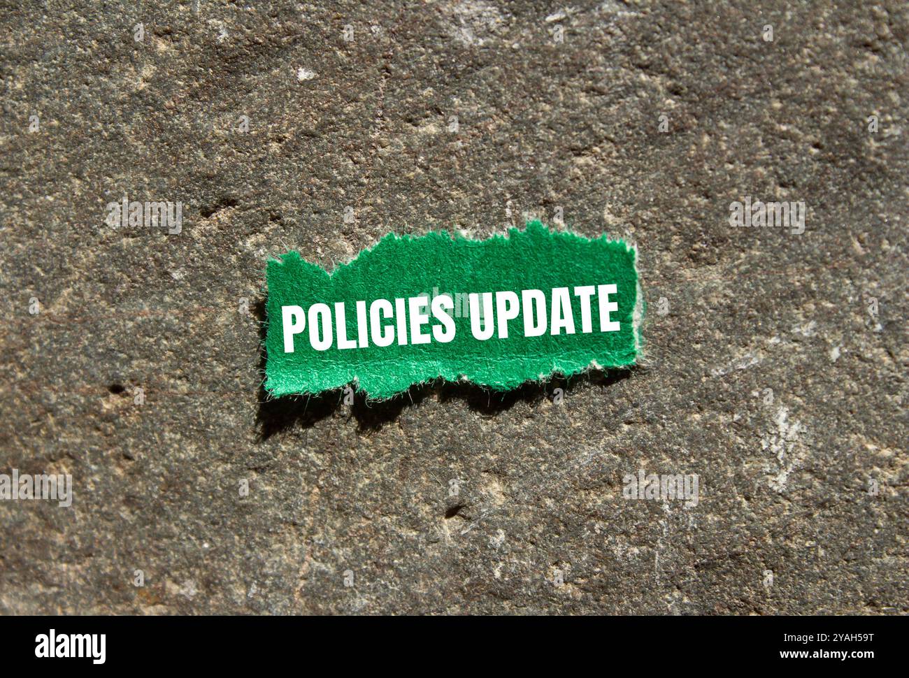 Policies update message written on ripped green torn paper piece with stone background ...