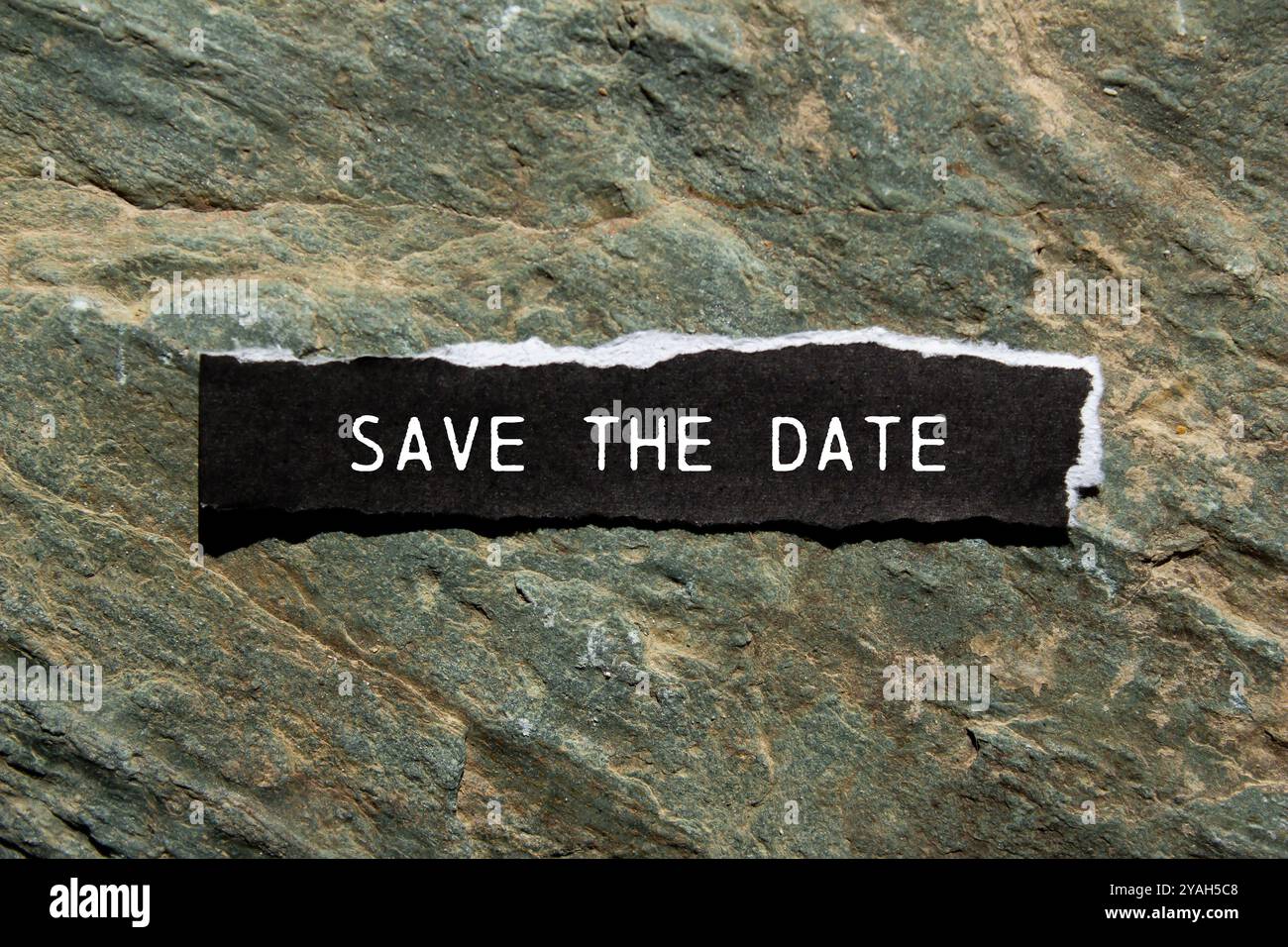Save the date message written on ripped black torn paper piece with stone background. Conceptual ...